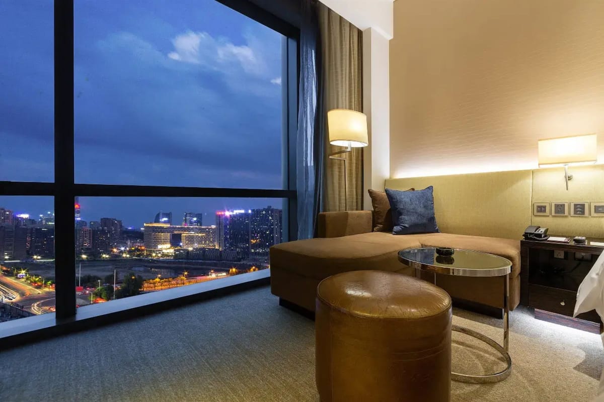 Quarto de hotel com uma janela grande, um sofá, uma mesa de centro e um abajur.