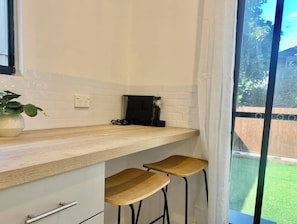 Uma cozinha com bancada de madeira, uma cafeteira e dois banquinhos.