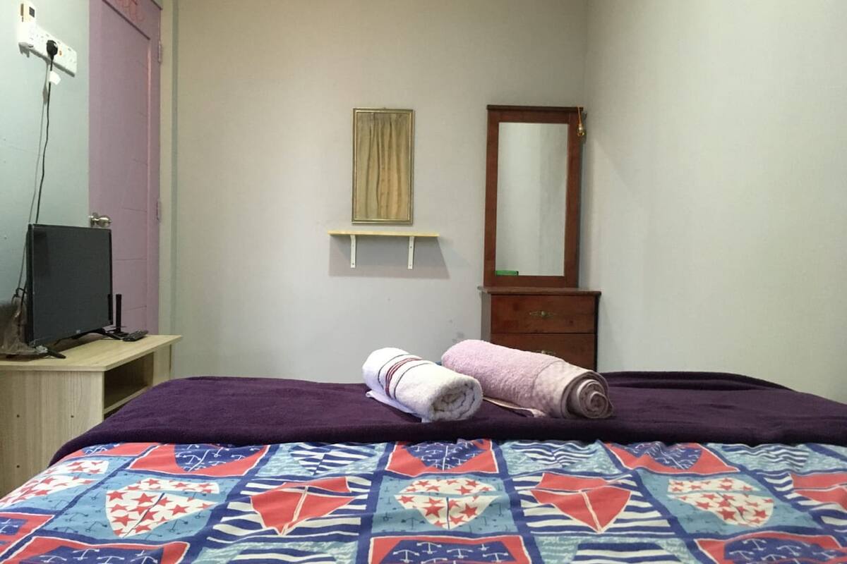 Quarto com cama, penteadeira, espelho, prateleira com cortina e TV sobre suporte.