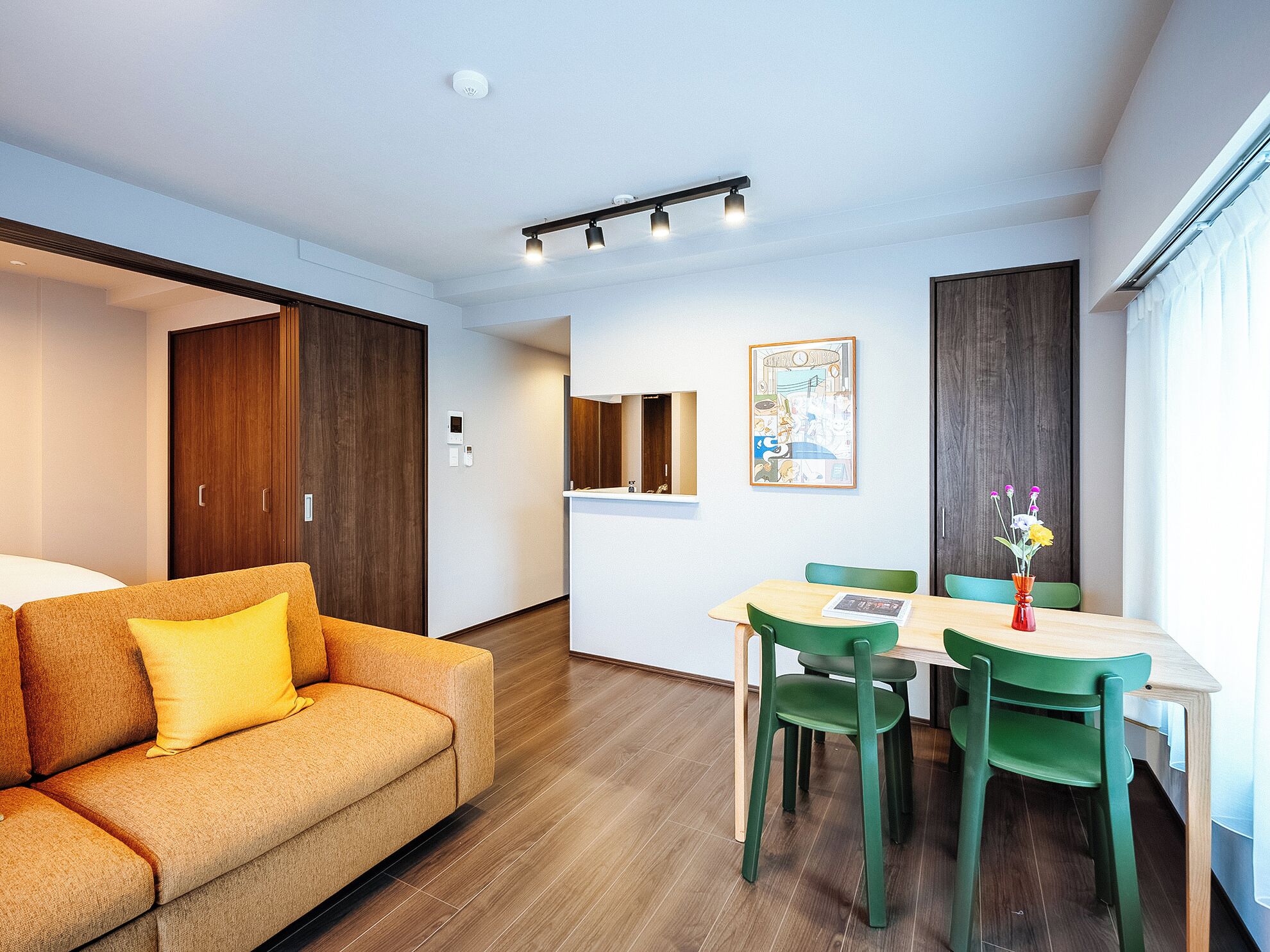 Quarto de hotel moderno com sofá, mesa de jantar, cadeiras e um quadro na parede.