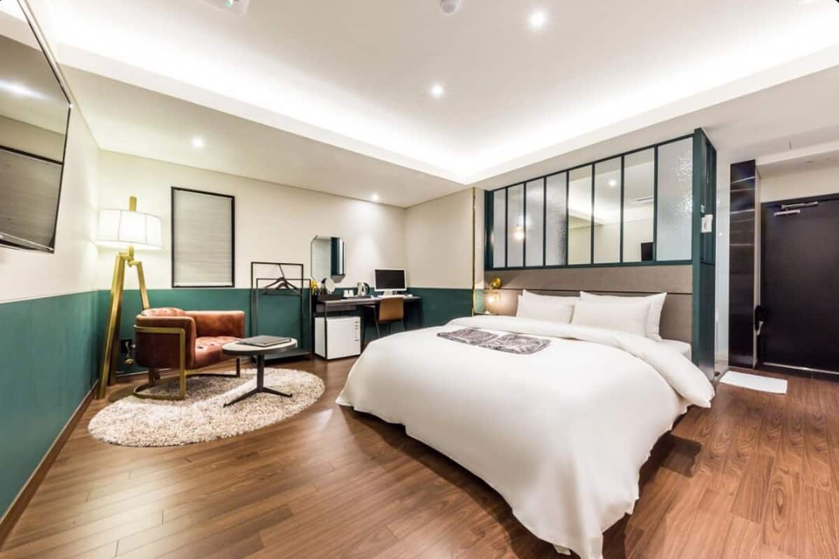 Quarto de hotel com uma cama grande, uma escrivaninha com computador, uma cadeira, um abajur e um espelho.