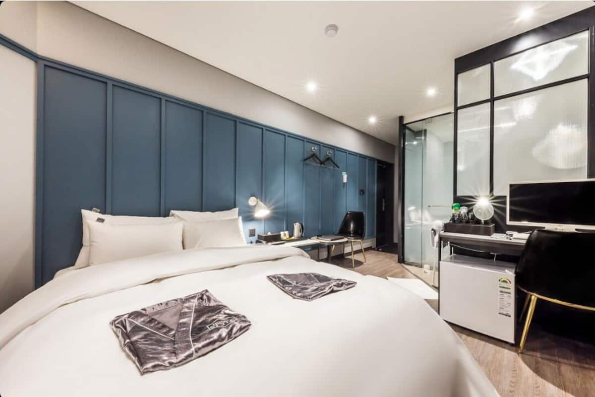 Quarto de hotel moderno com uma cama grande, uma escrivaninha com computador, uma TV e um guarda-roupa.