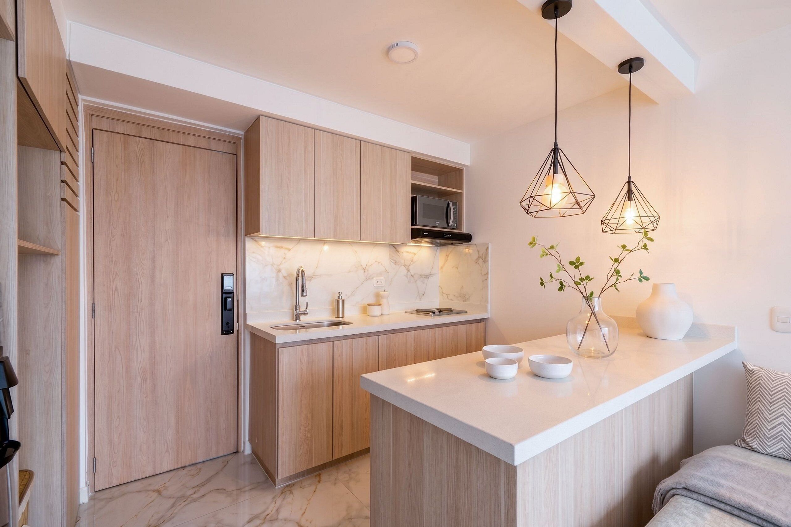 A modern kitchen with wooden cabinets, a marble countertop, a built-in microwave, and pendant lighting.