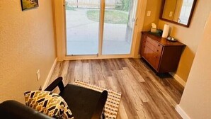Quarto com porta de vidro deslizante para o exterior, uma poltrona de couro preto, piso de madeira, um tapete pequeno e um armário de madeira com espelho.