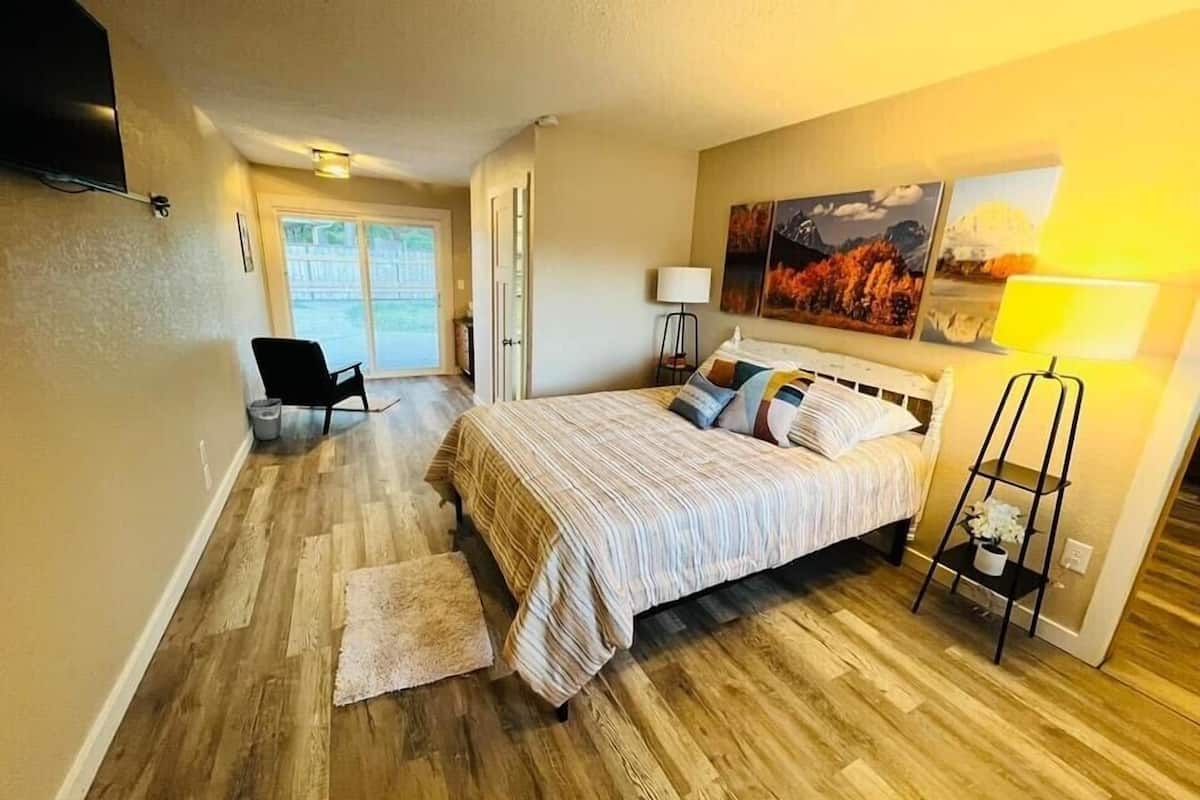 Quarto com cama, cadeira, abajur e um quadro na parede.