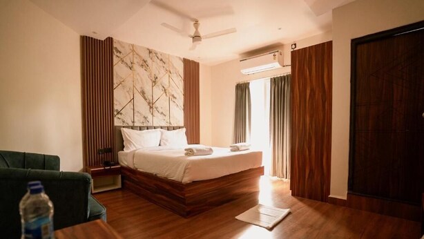 Quarto de hotel com cama, poltrona verde, piso de madeira, ventilador de teto e janela com cortinas.