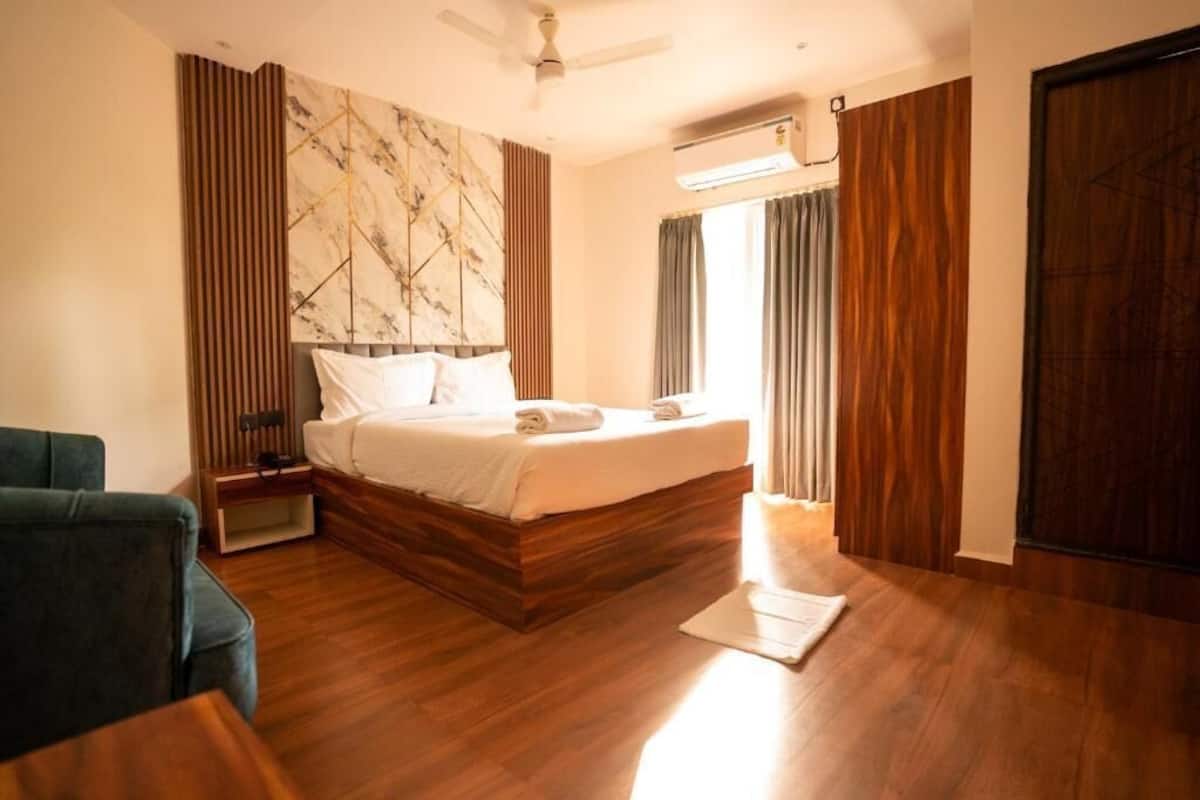 Um quarto com cama, mesa de cabeceira, cadeira, ventilador de teto e piso de madeira.