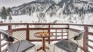 Varanda com mesa e duas cadeiras, com vista para uma paisagem montanhosa coberta de neve.
