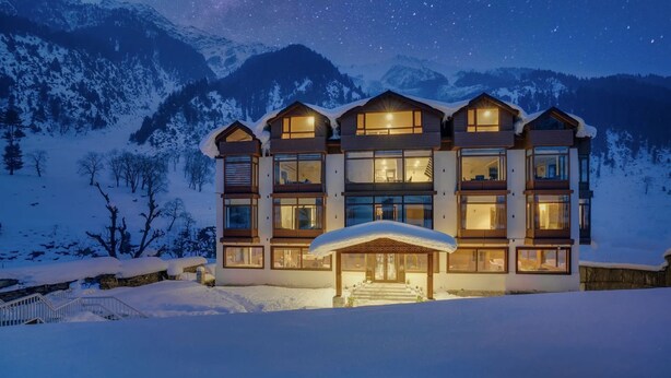 Um hotel com vários andares, entrada coberta de neve e vista para montanhas ao fundo.