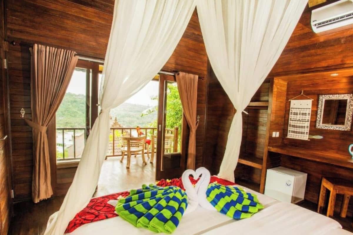 Quarto de madeira com uma cama, cortinas, uma mesa pequena e vista para o verde lá fora.