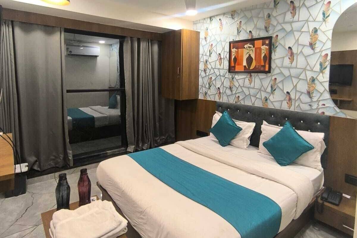 Quarto de hotel com cama, escrivaninha, cadeira, guarda-roupa, ventilador de teto e televisão na parede.