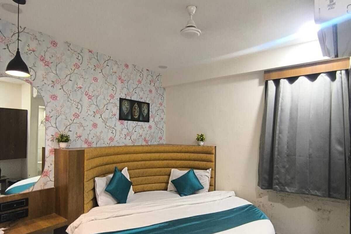 Quarto com cama redonda, cabeceira de madeira, mesa de cabeceira, espelho, papel de parede floral e janela com cortinas.