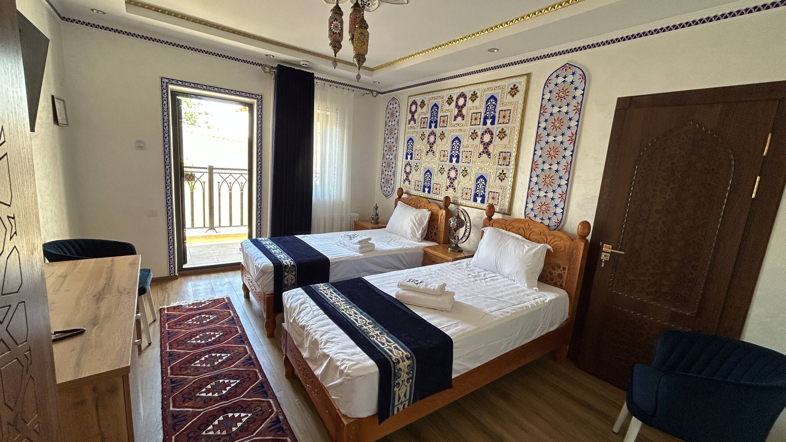 Quarto de hotel com duas camas, porta de madeira, parede com padrão e vista pela janela.