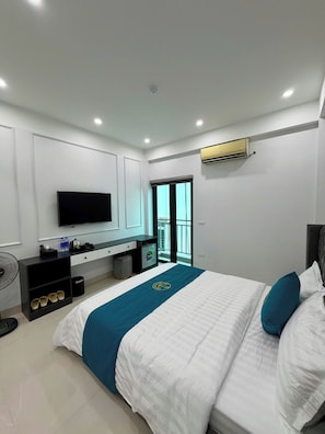 Quarto de hotel com cama, televisão, minibar, ventilador e ar condicionado.