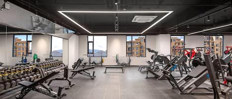 Uma academia moderna com diversos equipamentos de exercício, amplas janelas e vista para edifícios.