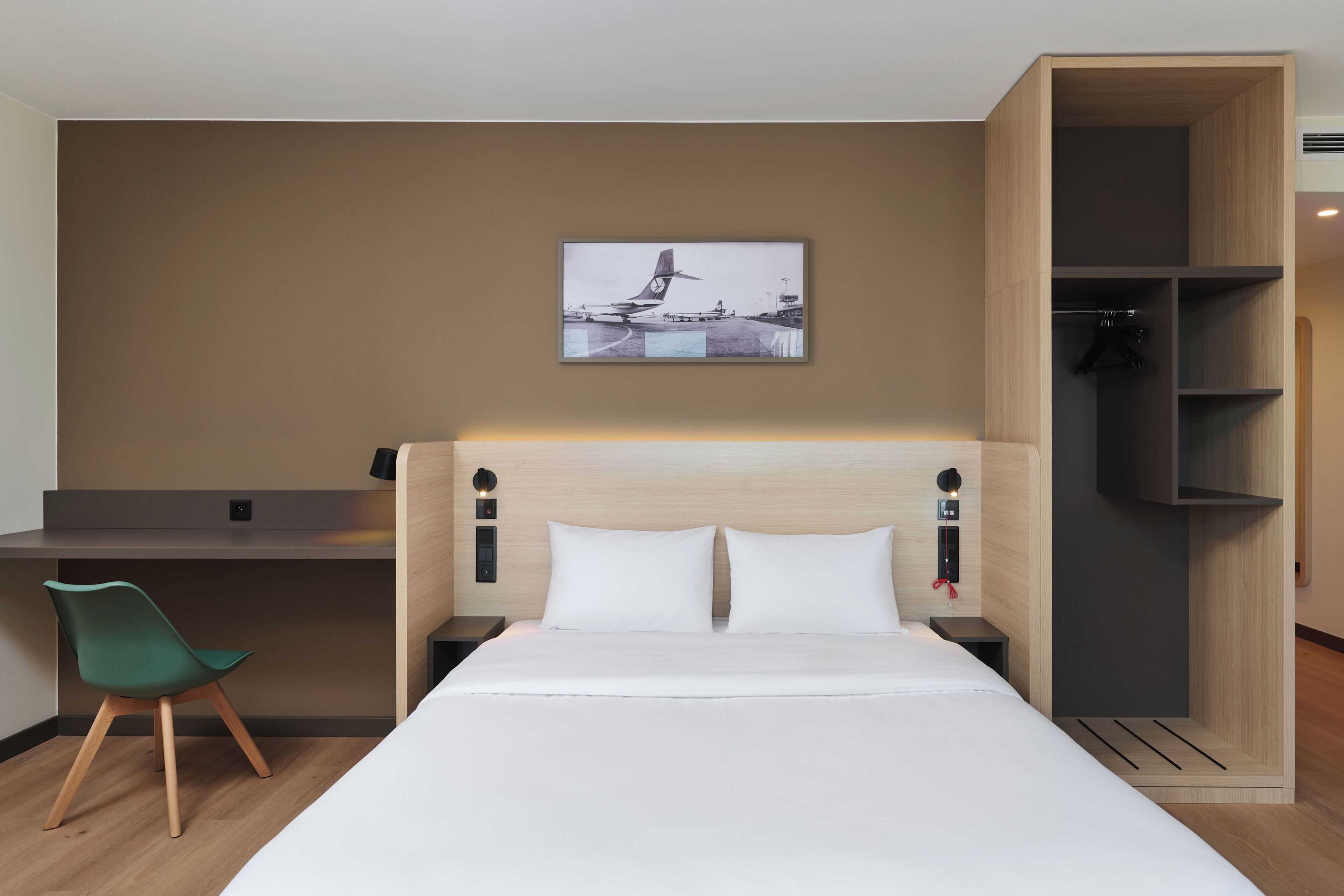 Quarto de hotel com cama, escrivaninha, cadeira, guarda-roupa e um quadro na parede.