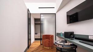 Quarto moderno com televisão de tela plana, escrivaninha com computador, cadeira e um banquinho pequeno.