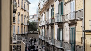 Uma rua estreita com edifícios altos, varandas e uma ponte visível.