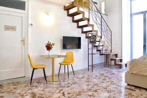 Interior moderno com escada, área de jantar com cadeiras amarelas, televisão e uma porta com placa.