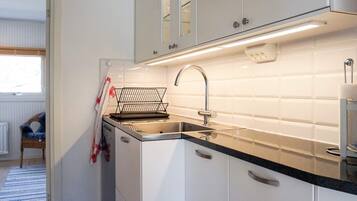 Cozinha compacta com armários brancos, pia de aço inoxidável e bancada preta.