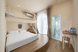Quarto com cama beliche, escrivaninha, cadeira, janela com cortinas e banheiro visível por uma porta de vidro.