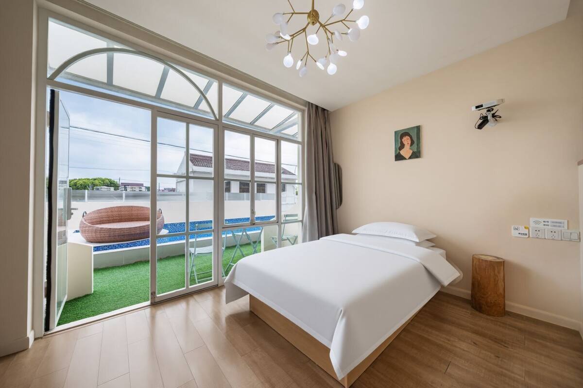 Quarto de hotel com cama, vista para uma piscina e uma grande porta de vidro que dá para o exterior.