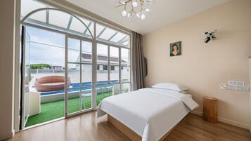 Quarto de hotel com cama, vista para uma piscina e uma grande porta de vidro que dá para o exterior.
