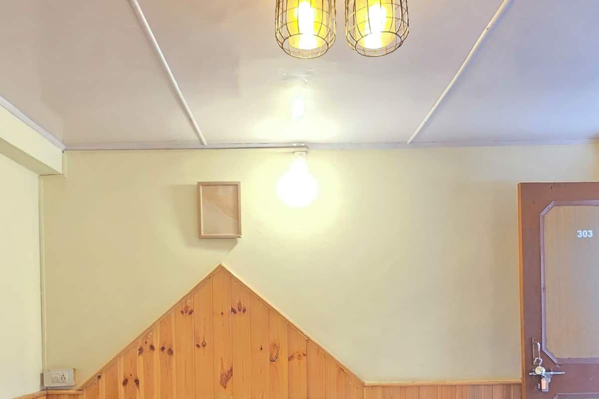 Quarto de hotel com cabeceira de madeira, cama com roupa de cama florida e duas luminárias suspensas.