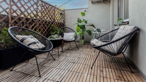 Um pátio externo com duas cadeiras de vime preto, uma mesinha e plantas em vasos.