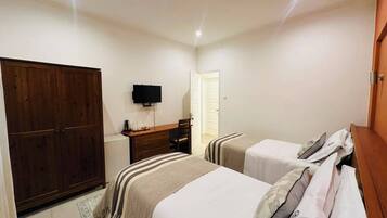 Quarto com duas camas, um guarda-roupa, uma escrivaninha com televisão e uma porta que dá para outro cômodo.