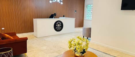 Uma área de recepção de hotel com balcão, sofá, mesa de centro e planta decorativa.