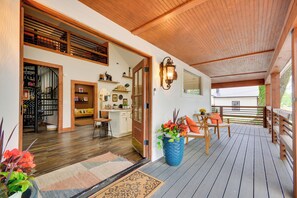 Um deck de madeira com área de estar externa, um vaso grande com planta e uma porta que dá para um espaço interior com cozinha e sala de jantar.