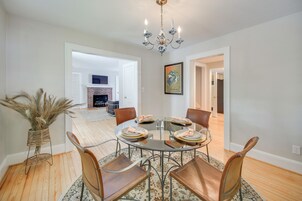 Uma sala de jantar com mesa de vidro, cadeiras de couro, lustre e lareira ao fundo.
