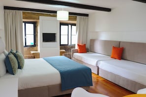 Quarto de hotel com uma cama, dois sofás, televisão e janela com cortinas.