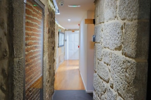 Um corredor com paredes de pedra, piso de madeira e uma porta no final.