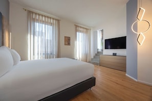 Quarto de hotel moderno com uma cama grande, televisão de tela plana na parede e uma escada para um andar superior.