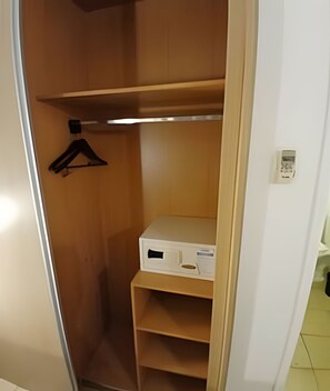 Um armário de madeira com uma barra para pendurar roupas e um dispositivo eletrônico branco numa prateleira.