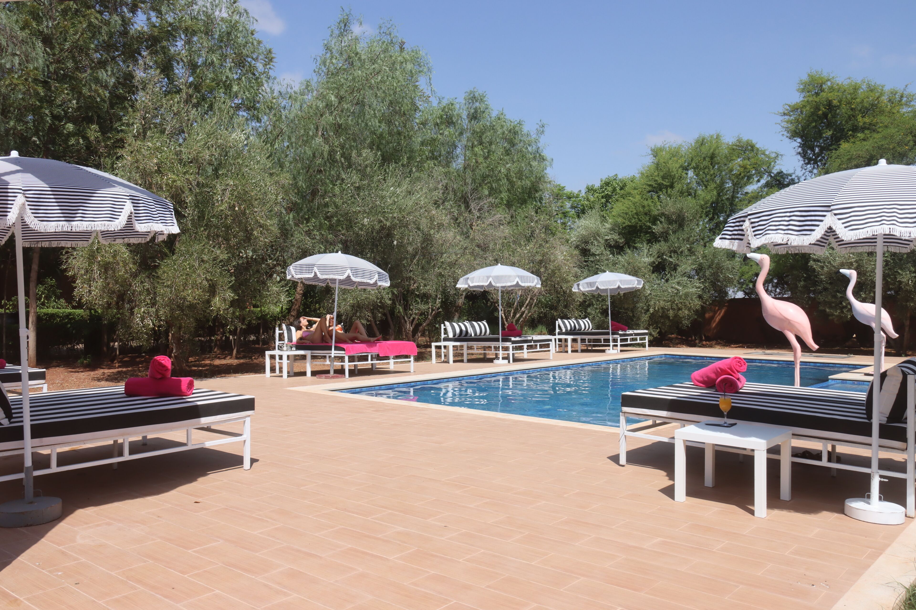 Área de piscina com espreguiçadeiras e guarda-sóis, cercada por árvores.