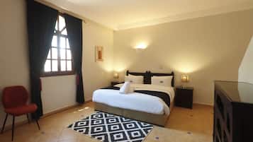 Quarto de hotel com cama, luminárias de cabeceira, uma cadeira vermelha, tapete estampado e um quadro na parede.