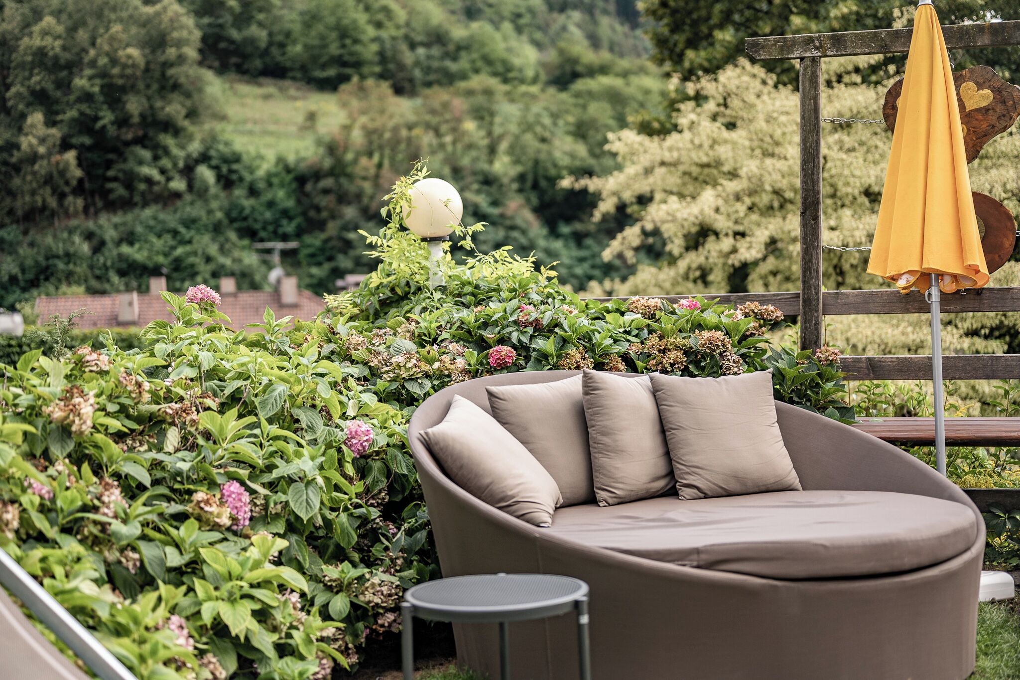 Um jardim com um espaço de estar externo circular, uma pequena mesa redonda e um guarda-sol amarelo.