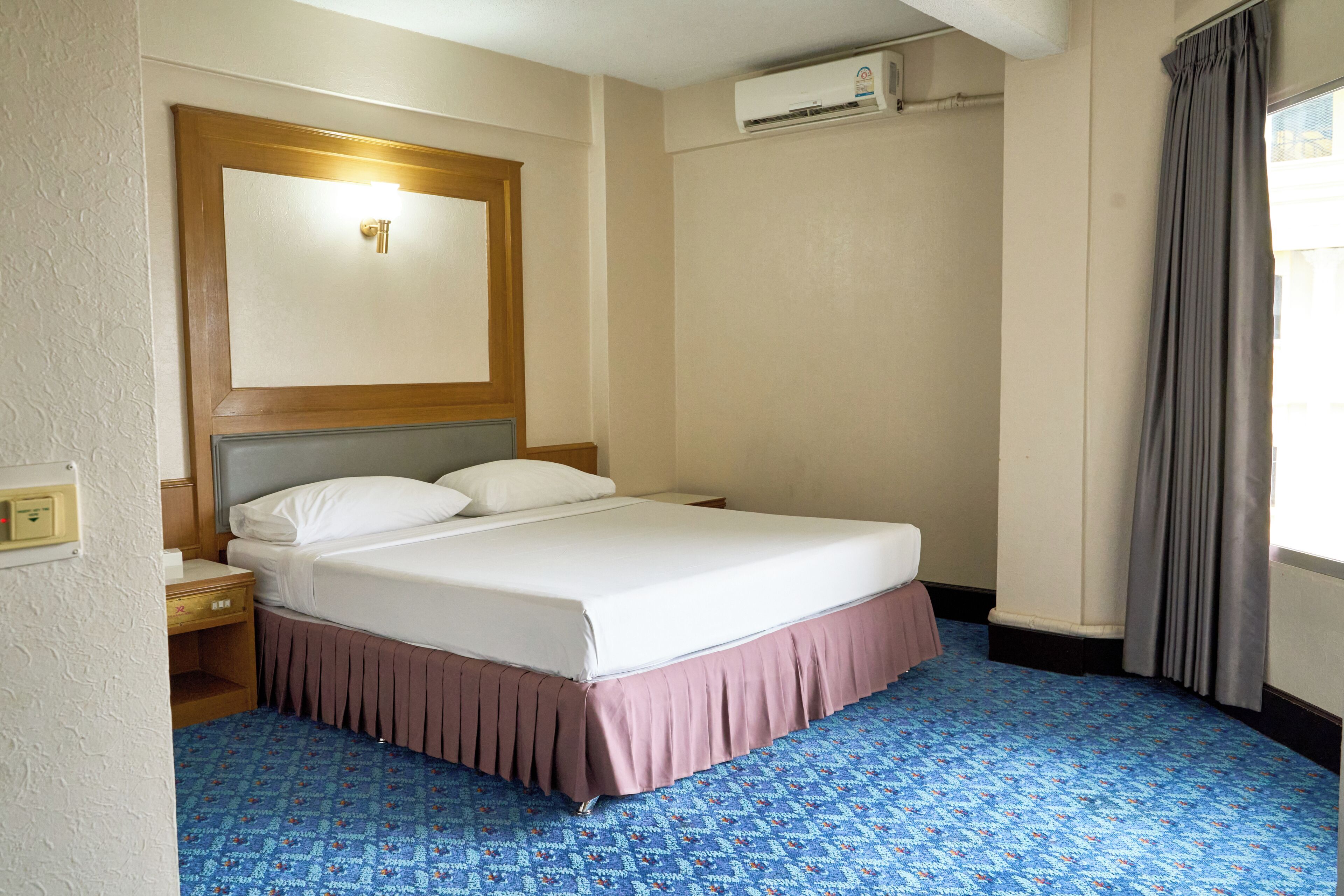 Quarto de hotel com uma cama, mesa de cabeceira, ar condicionado e janela com cortinas.