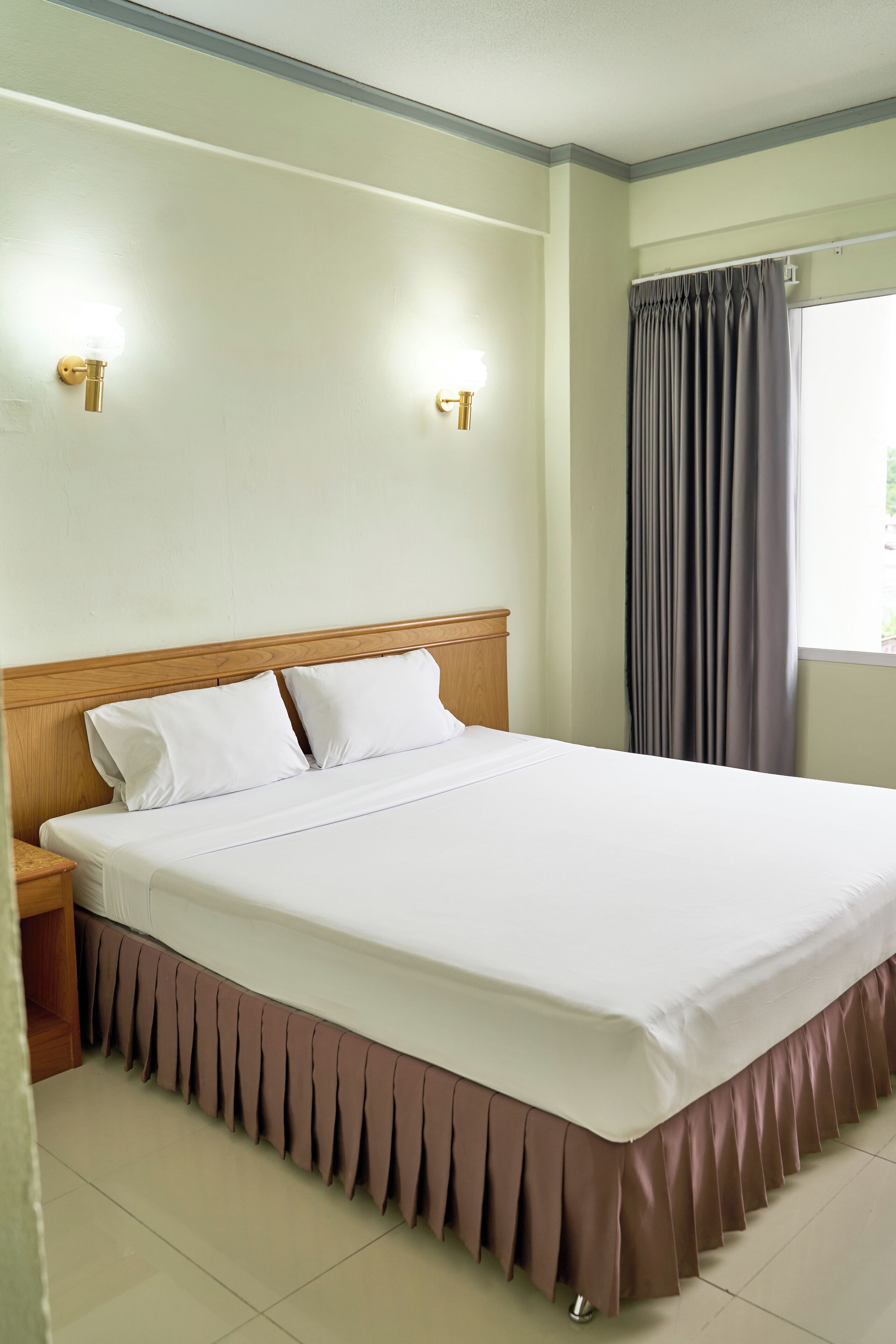Uma cama bem arrumada com cabeceira de madeira, mesa de cabeceira e uma janela com cortinas.