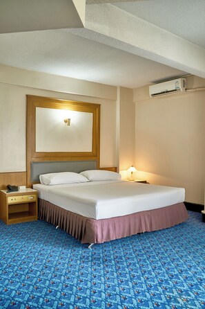 Quarto de hotel com cama, mesa de cabeceira, luminária e ar condicionado.