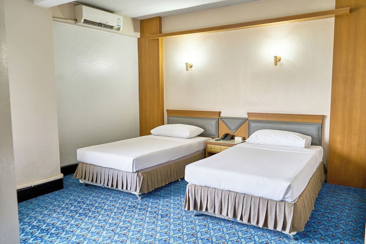 Quarto de hotel com duas camas de solteiro, mesa de cabeceira, telefone e ar condicionado fixado na parede.