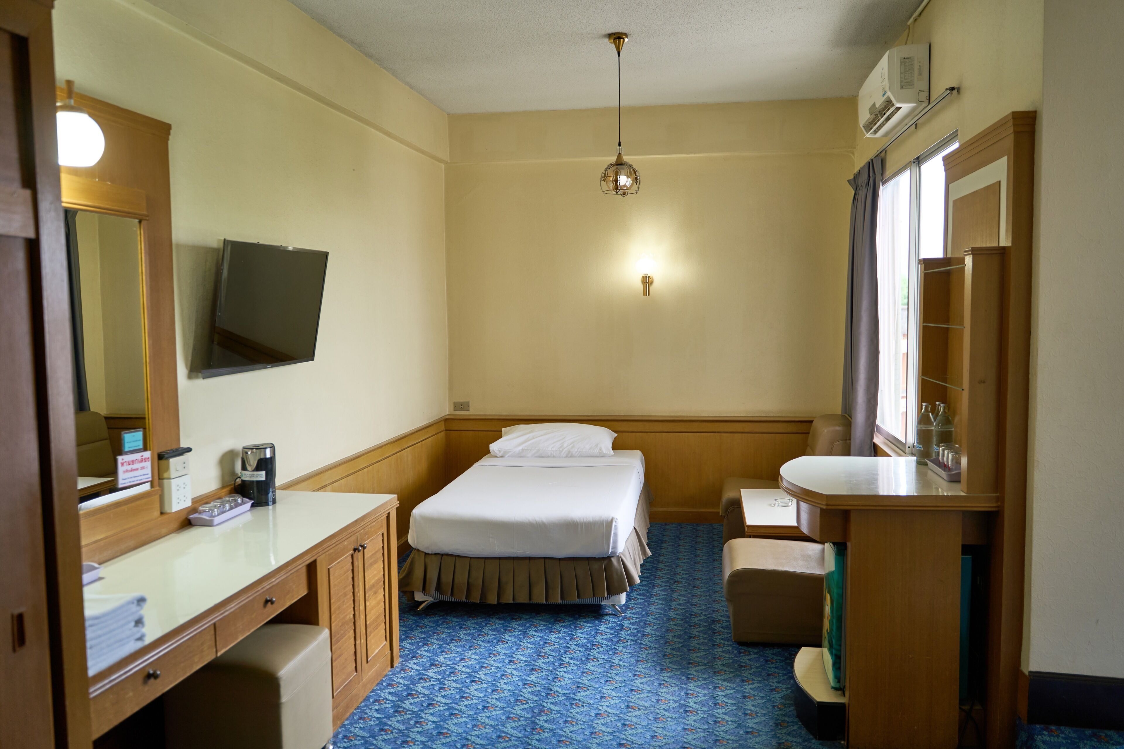 Quarto de hotel com cama, mesa de cabeceira, espelho e pequena escrivaninha com cadeira.