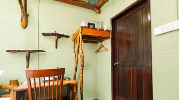 Quarto com cadeira de madeira, mesa, porta e prateleira fixada na parede com um micro-ondas.