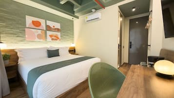 Quarto de hotel com uma cama, uma cadeira verde, uma mesa de madeira e obras de arte na parede.
