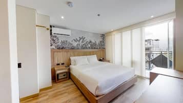 Quarto moderno com uma cama grande, cabeceira de madeira, mesa de cabeceira e vista para a cidade através de amplas janelas.