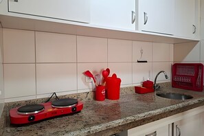 Cozinha com armários brancos, bancada de granito, fogão por indução vermelho e cesto de roupa vermelho.