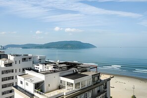 Vista costeira com edifícios modernos, uma praia e uma ilha ao longe.
